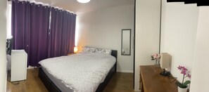 Quarto com cama, mesa de cabeceira, abajur, espelho, cômoda e planta em vaso.