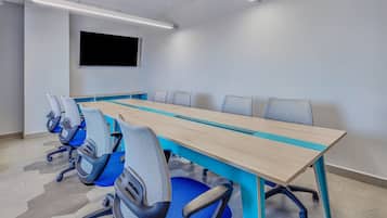 Uma sala de conferência com uma mesa comprida, cadeiras azuis e uma televisão de tela plana na parede.