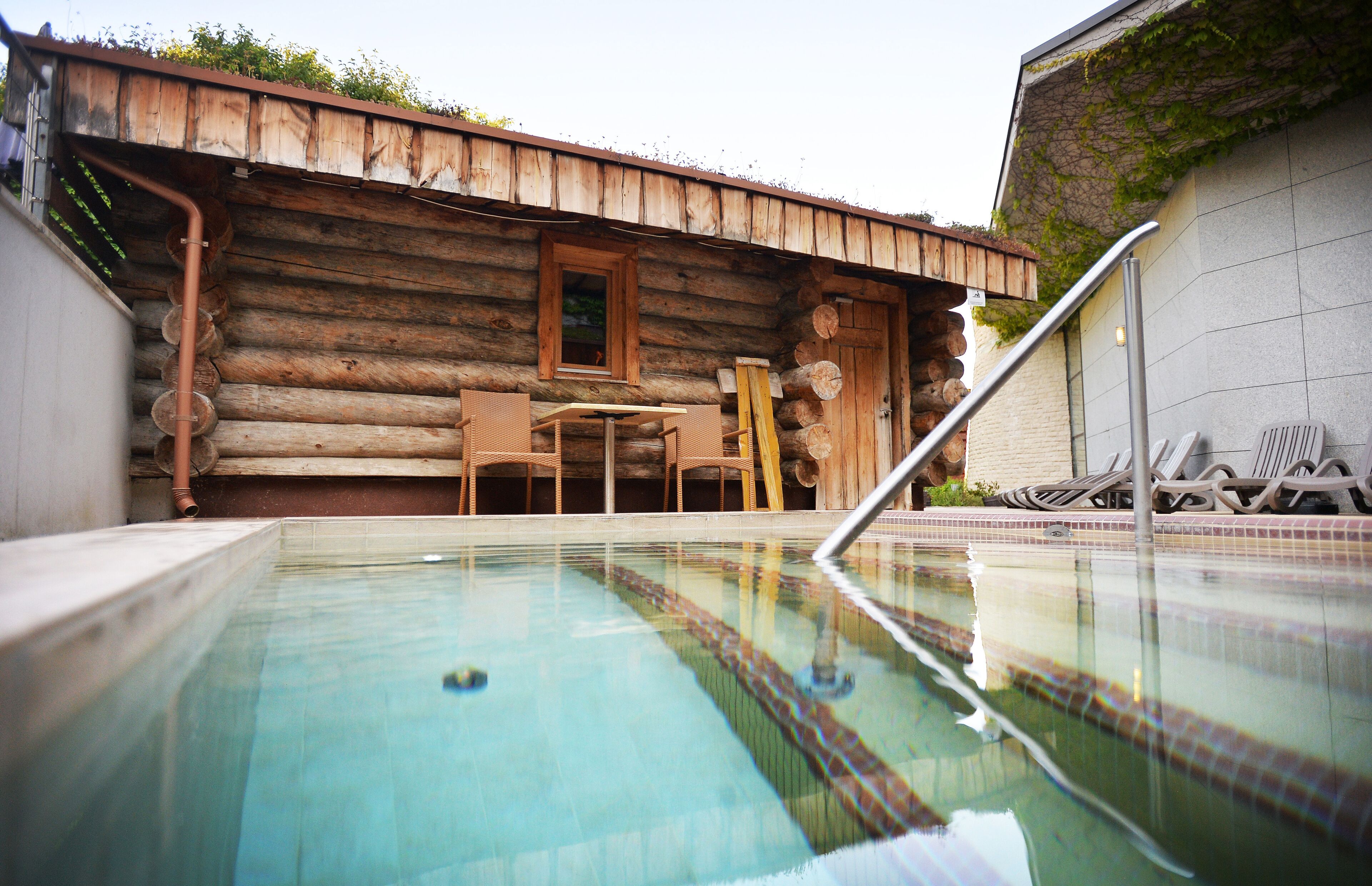 Uma área de piscina com estrutura de cabana de madeira, uma mesa e cadeiras de descanso.