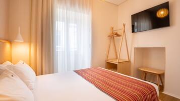 Quarto de hotel com cama, televisão na parede, cadeira de madeira e mesa pequena.