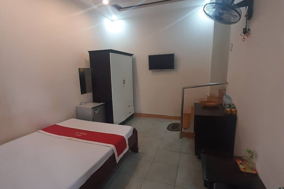 Quarto de hotel com cama, guarda-roupa, secretária, cadeira, televisão e ventoinha no teto.