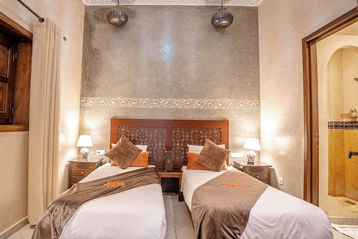 Quarto de hotel com duas camas, uma cabeceira grande e elaborada e um teto decorativo.