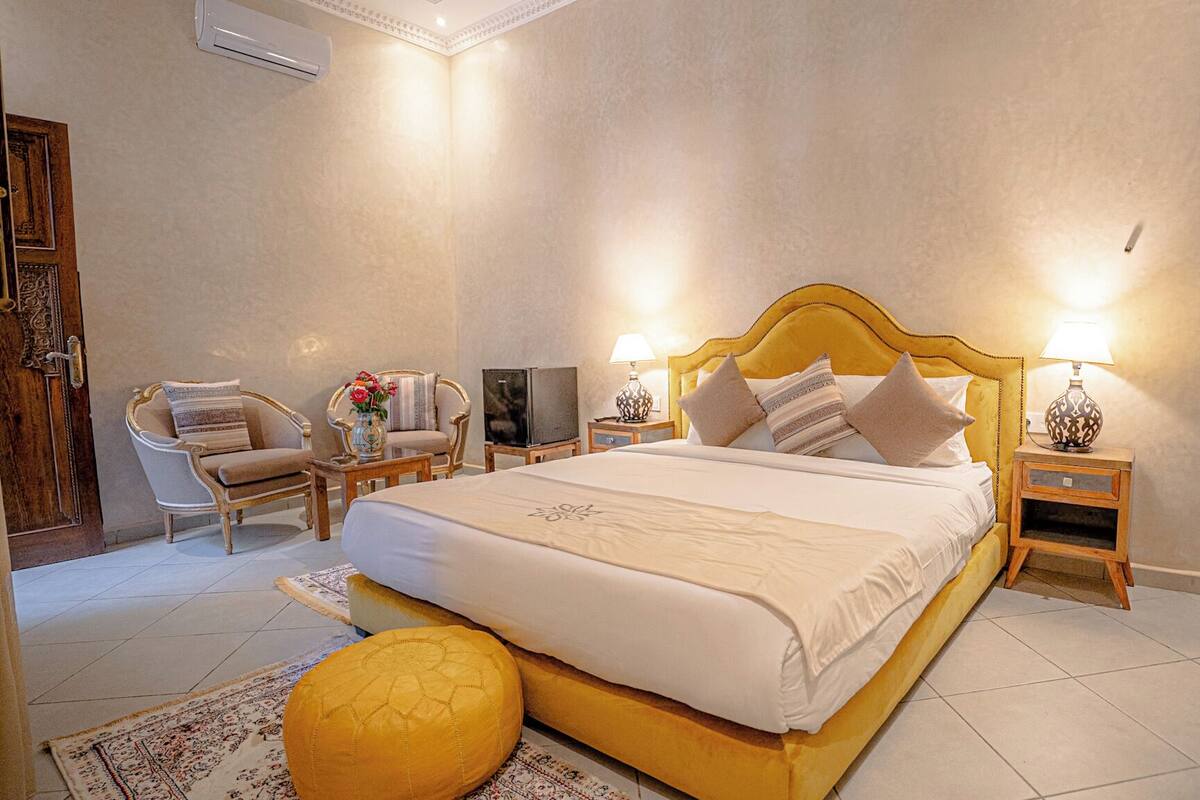 Quarto de hotel com uma cama, duas mesas de cabeceira, uma televisão, uma cadeira e um painel decorativo na parede.