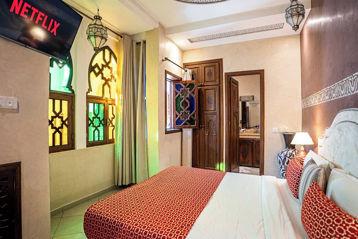 Quarto de hotel com cama, televisão presa na parede, guarda-roupa e casa de banho visível por uma porta aberta.