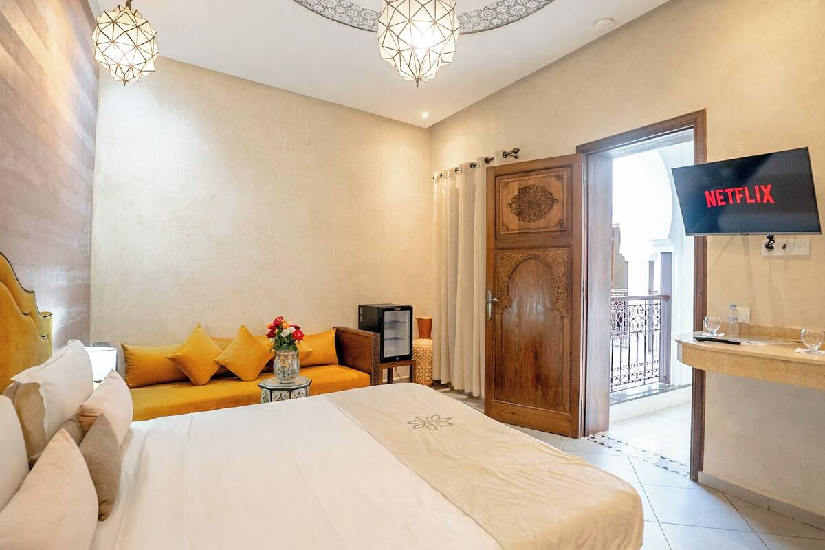 Quarto de hotel com cama, televisão, sofá e porta para uma varanda.
