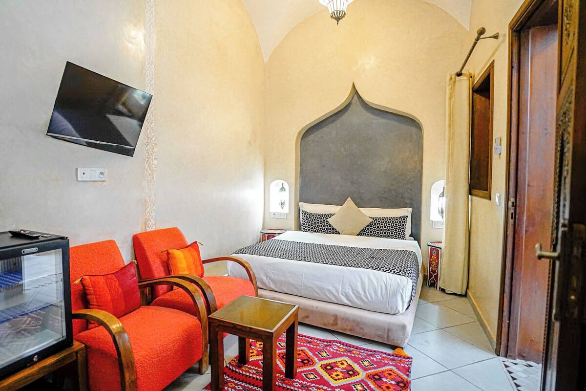 Quarto de hotel com cama, televisão, sofá e uma mesinha.
