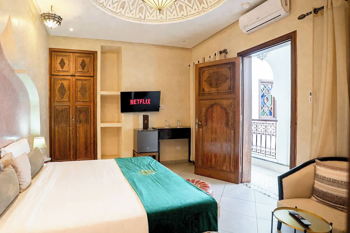 Quarto de hotel com cama, televisão, escrivaninha e varanda.