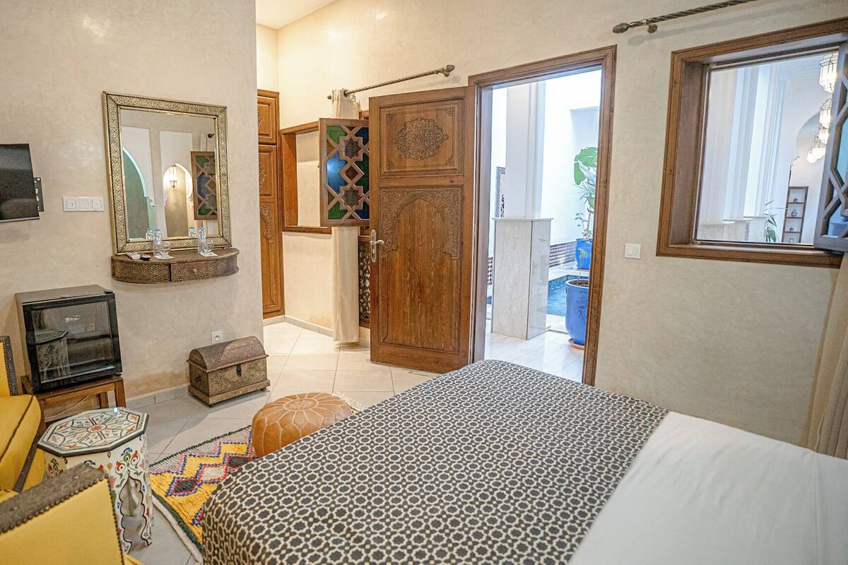 Quarto com cama, televisão, espelho, guarda-roupa e vista para o exterior.