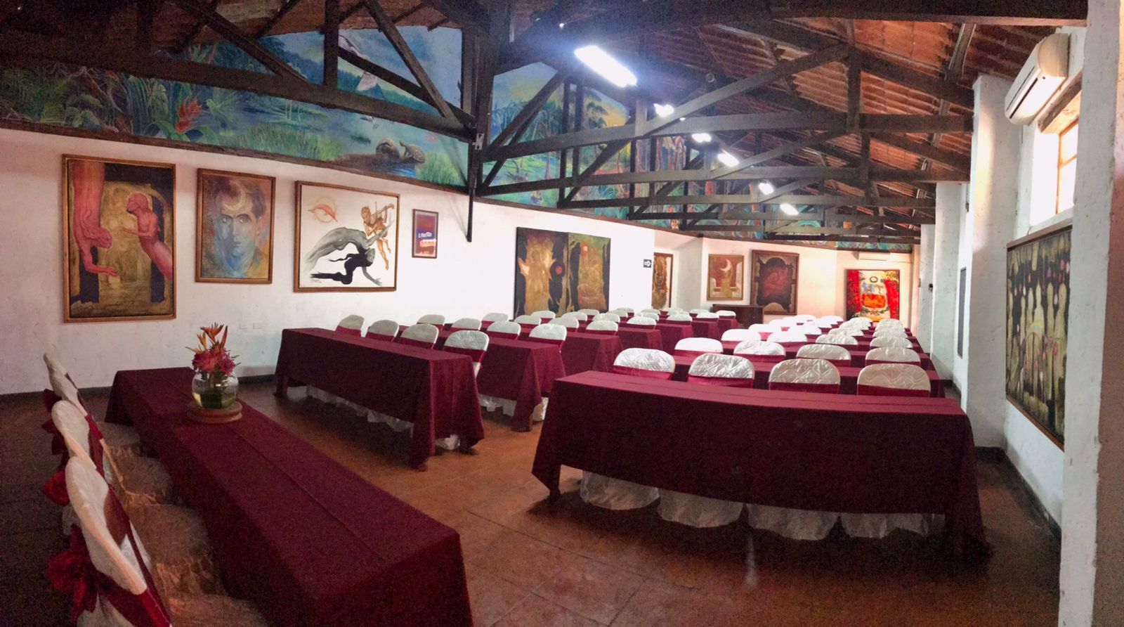 Um espaço com várias mesas cobertas por toalhas vermelhas, dispostas em fileiras.