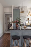 Cozinha moderna com bancada de mármore, dois banquinhos, luminária pendente e um vaso com flores.