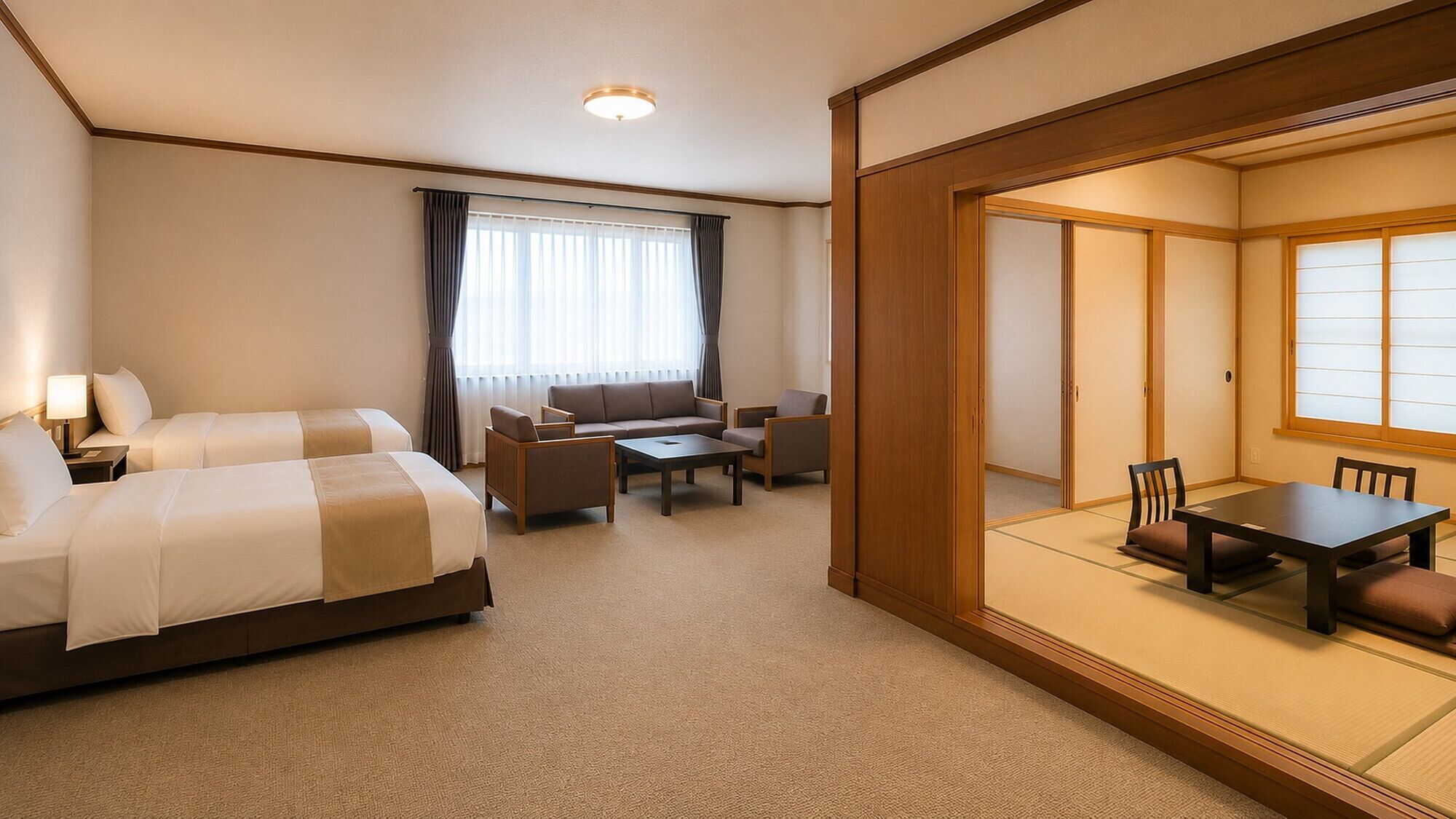 Quarto de hotel com duas camas, um sofá, uma mesa de jantar com cadeiras e uma porta deslizante que dá para outro cômodo.