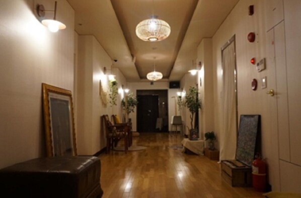 Um corredor com piso de madeira, um candelabro, quadros nas paredes e uma porta no final.
