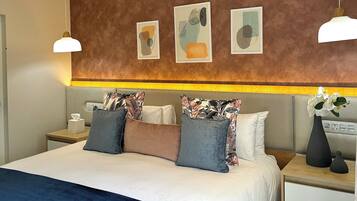 Quarto de hotel moderno com uma cama grande, duas mesas de cabeceira, um criado-mudo, unidade de ar condicionado e obras de arte na parede.
