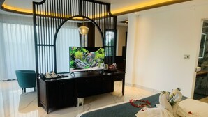 Quarto de hotel moderno com uma cama grande, uma TV sobre um console de madeira escura, uma cadeira azul e um painel decorativo na parede.