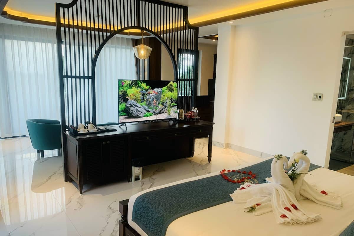 Quarto de hotel moderno com uma cama grande, uma TV sobre um console de madeira escura, uma cadeira azul e um painel decorativo na parede.