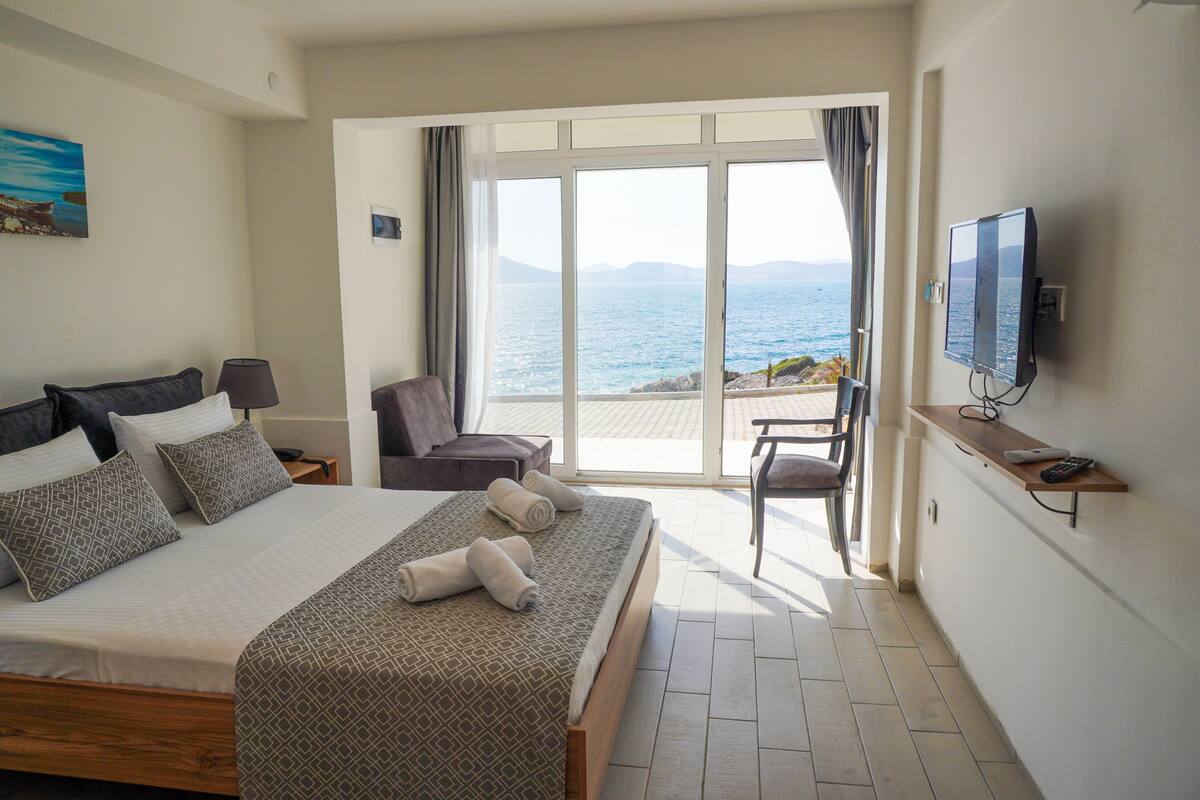 Quarto de hotel com cama grande, televisão, cadeira e vista para o mar.