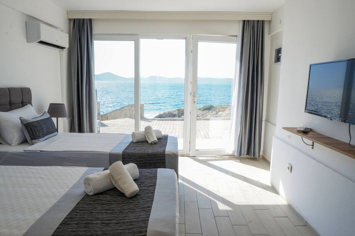 Quarto de hotel com duas camas, televisão e vista para o mar.