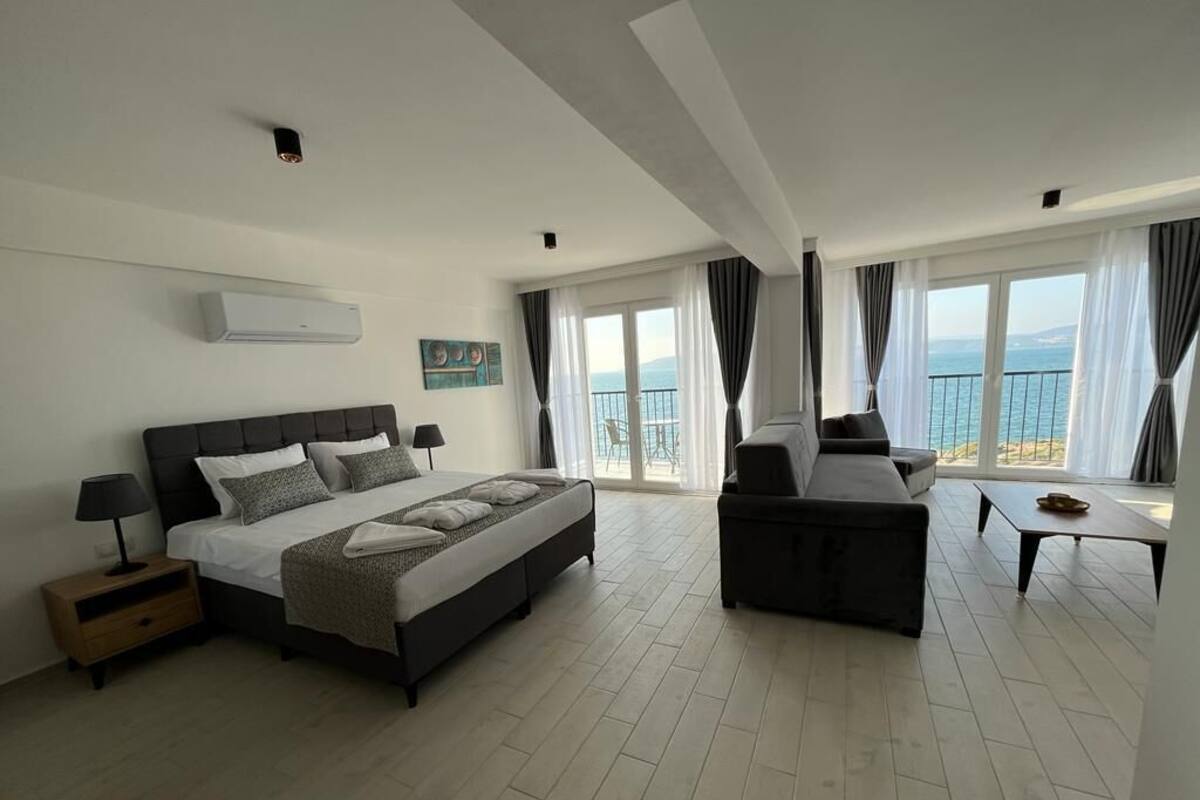 Quarto de hotel moderno com uma cama grande, um sofá, uma mesa pequena e uma varanda com vista para o mar.