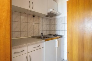 Uma cozinha com armários brancos, pia de aço inoxidável e forno embutido.