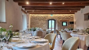 Um restaurante com mesas redondas preparadas para refeições, paredes de pedra e vigas de madeira.