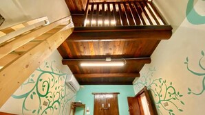Quarto com teto de madeira, cama com roupa de cama branca, porta de madeira e parede com estampas florais verdes.