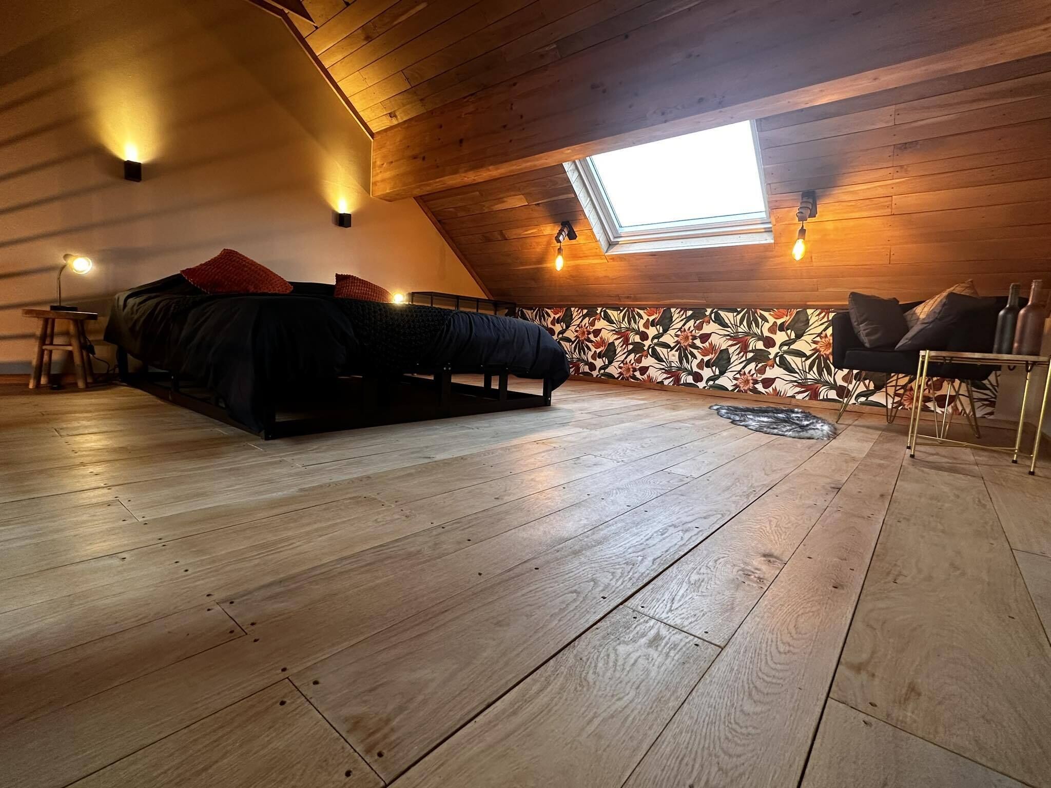 Um quarto de sótão aconchegante com cama beliche, piso de madeira, claraboia e parede com padrão floral.