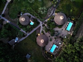 Vista aérea de um resort com três estruturas de telhado arredondado, uma piscina e um jardim bem cuidado.