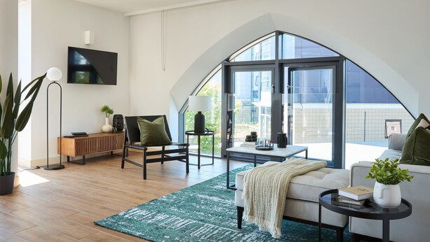 Uma sala de estar moderna com uma grande janela em arco, um sofá, uma mesa de centro e uma televisão fixada na parede.