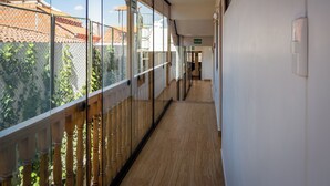 Um corredor com paredes de vidro, piso de madeira e vista para um telhado vermelho lá fora.