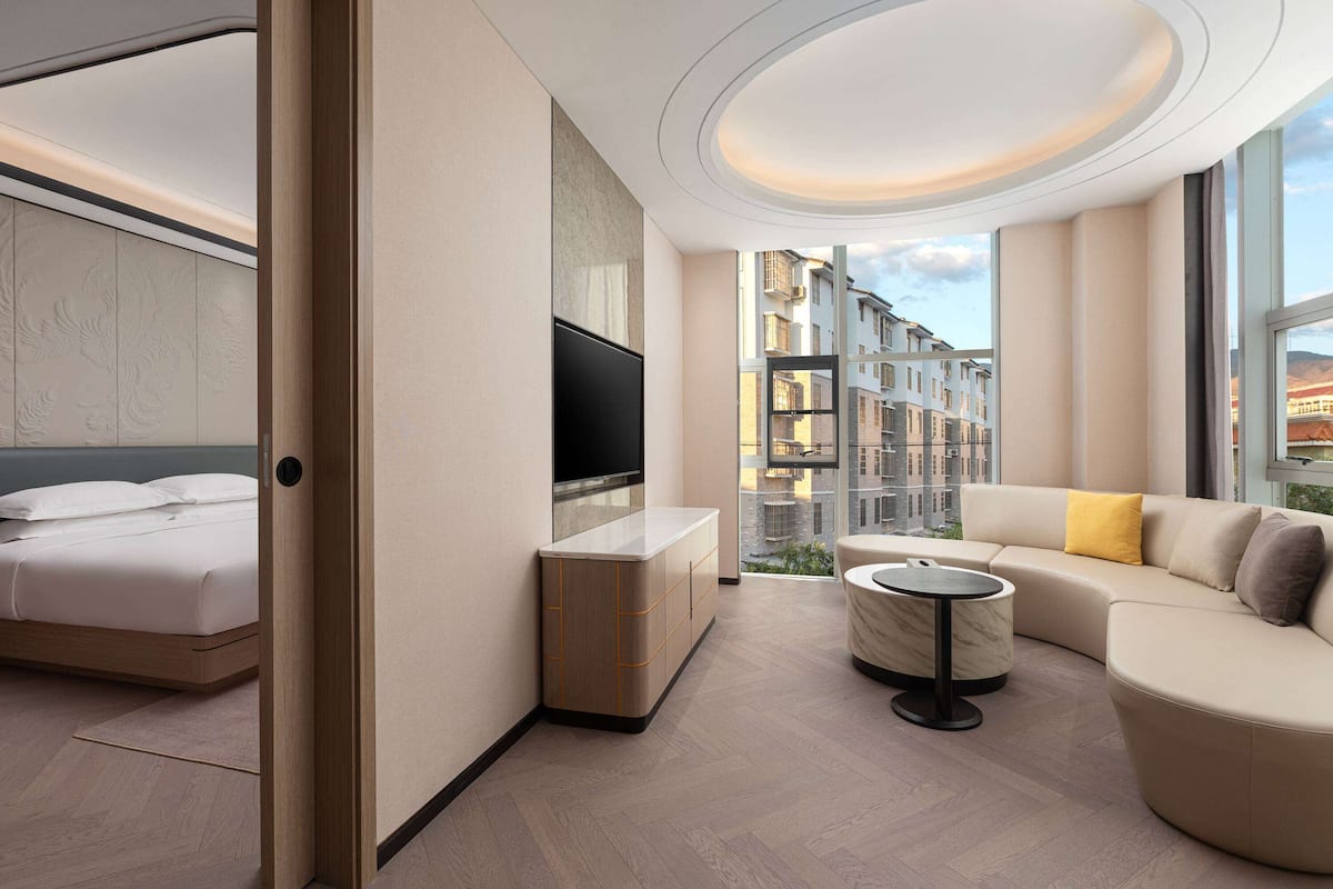 Quarto de hotel moderno com cama, sofá, televisão e vista para a cidade.