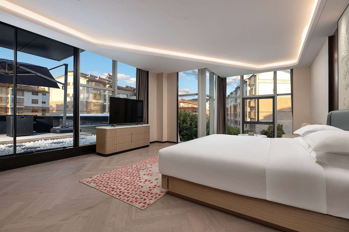 Quarto moderno com cama grande, TV e vista para a cidade através de amplas janelas.