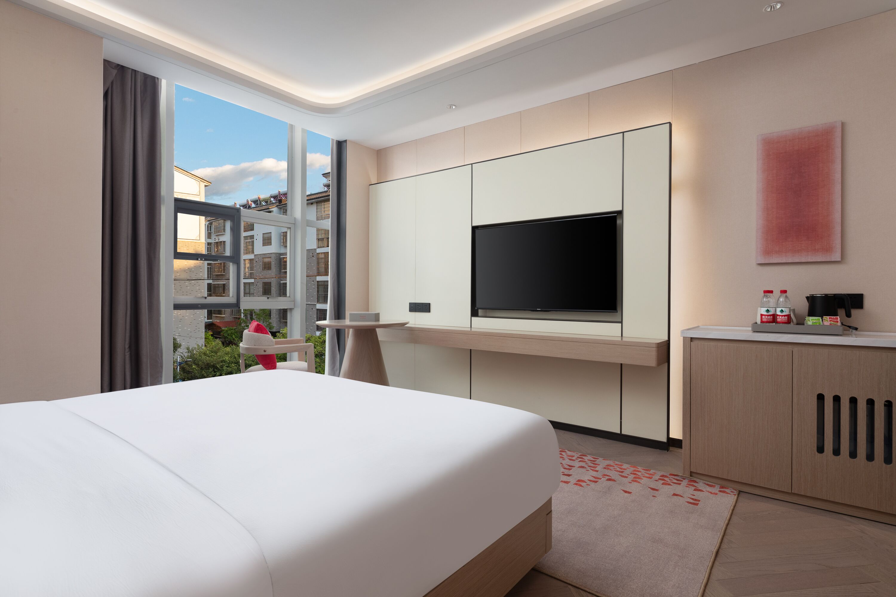 Quarto de hotel moderno com uma cama grande, televisão de tela plana, minibar e vista para a cidade pela janela.