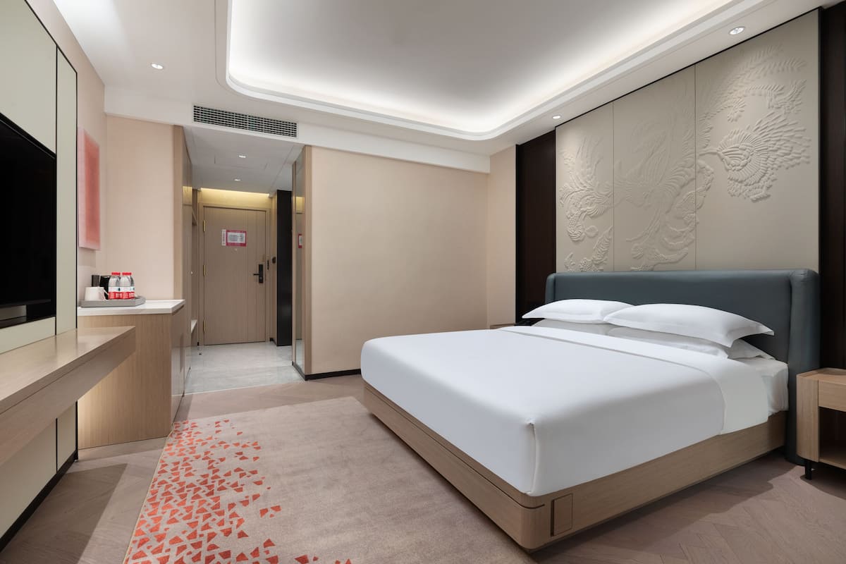 Quarto de hotel moderno com uma cama grande, televisão de tela plana, mesa de cabeceira e painel decorativo na parede.