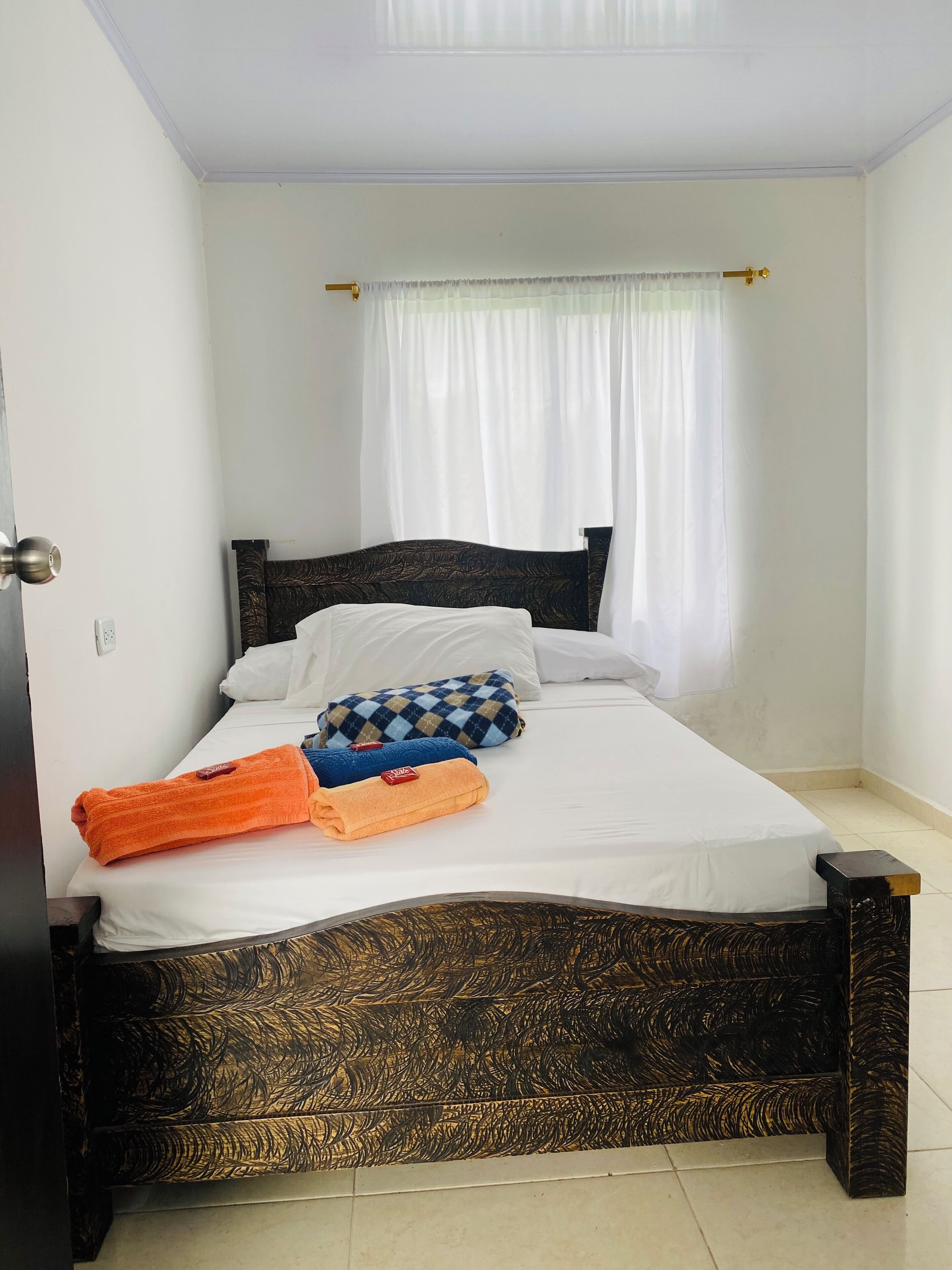 Uma cama de solteiro com cabeceira estampada escura, roupa de cama branca e duas almofadas (uma com padrão xadrez).