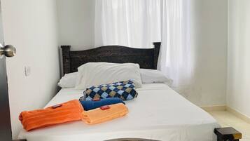 Uma cama de solteiro com cabeceira estampada escura, roupa de cama branca e duas almofadas (uma com padrão xadrez).