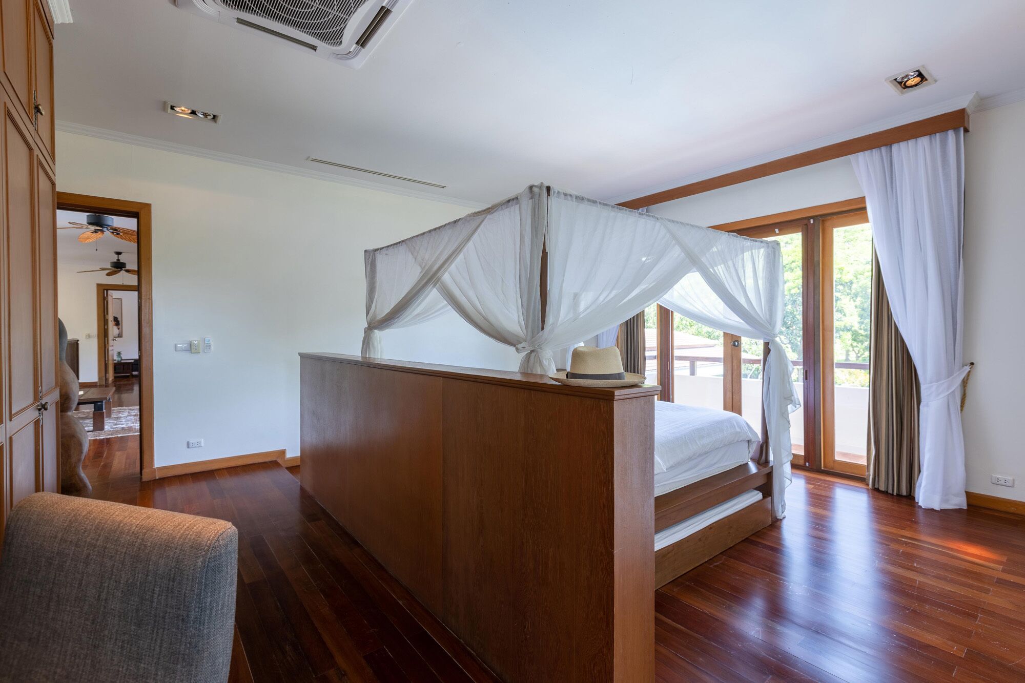 Quarto com cama de madeira, dossel e vista para o exterior.