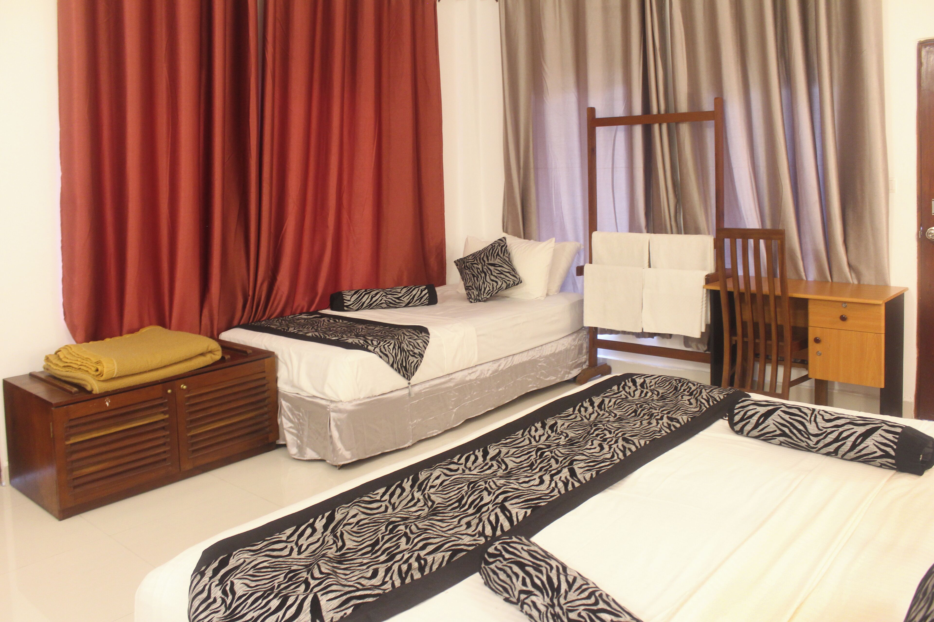 Quarto com uma cama, mesa de cabeceira de madeira, escrivaninha e uma cadeira.
