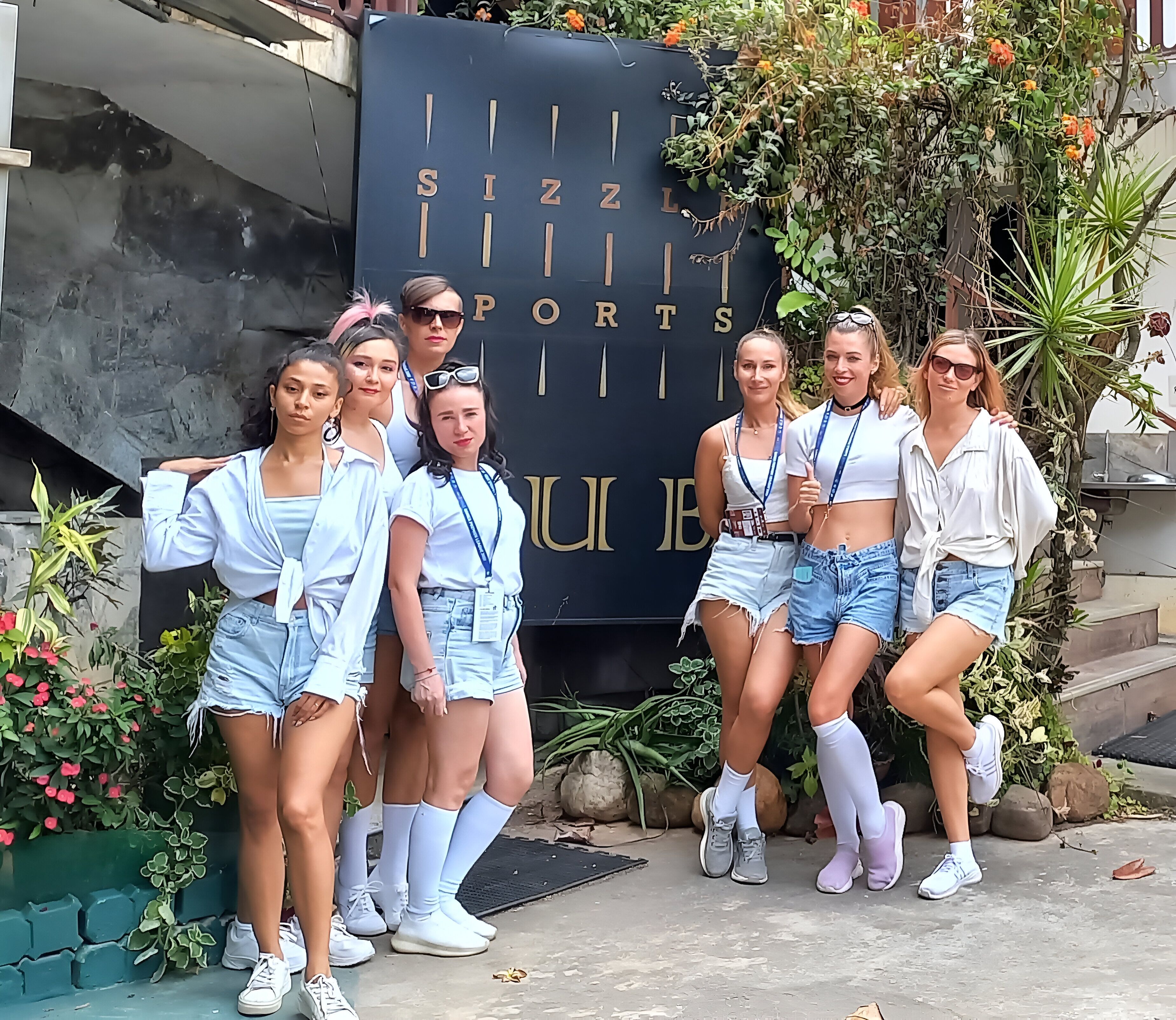 Um grupo de pessoas posando em frente a uma placa com o texto "SIZZL SPORTS".