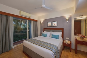 Quarto de hotel com uma cama grande, uma mesa de cabeceira com telefone, um espelho e vista para o verde através de uma porta deslizante.