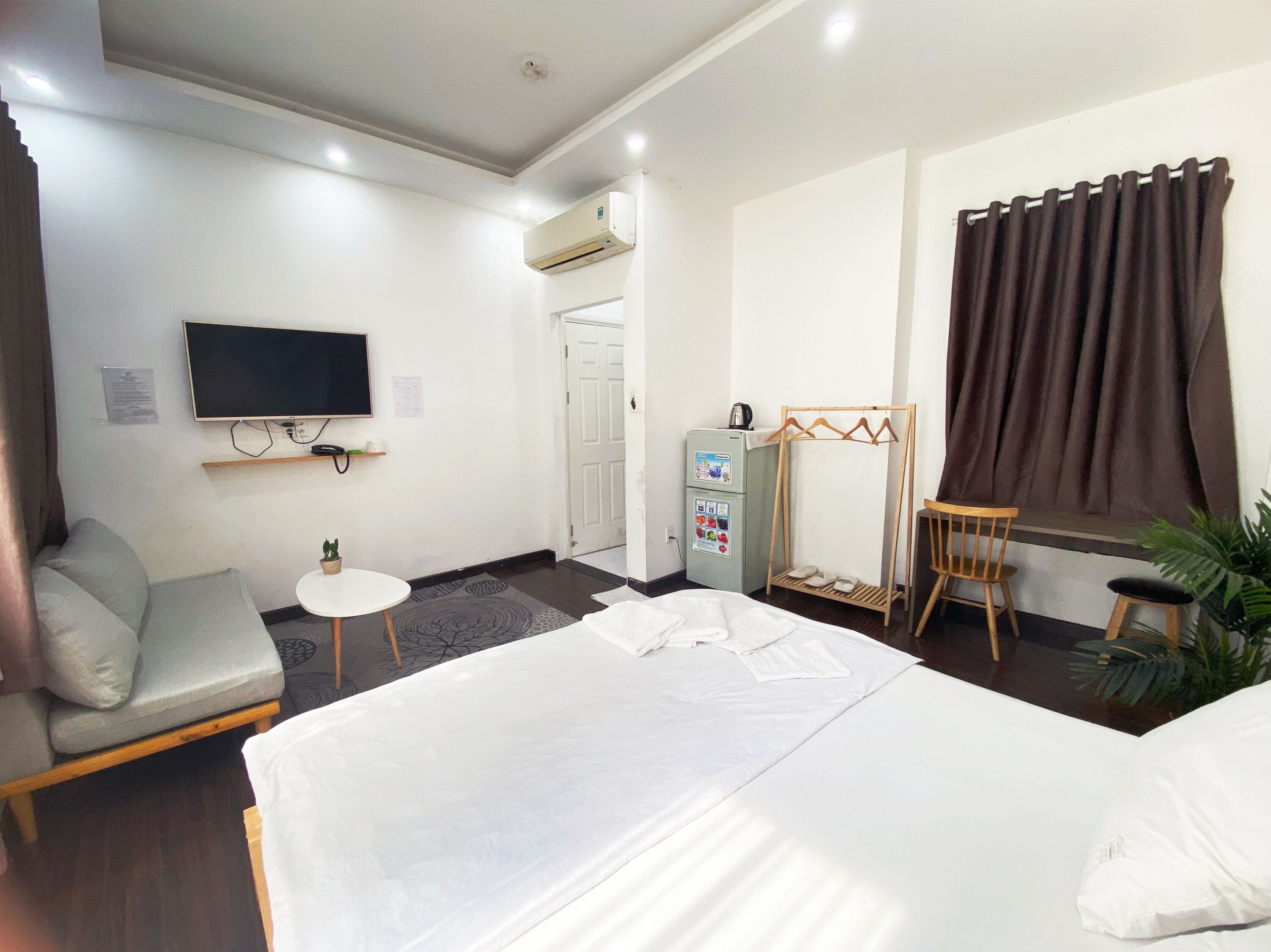Quarto de hotel com cama, televisão, mesa pequena, sofá, guarda-roupa e janela com cortinas.