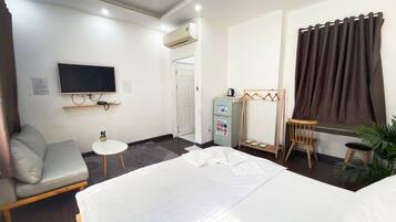 Quarto de hotel com cama, televisão, mesa pequena, sofá, guarda-roupa e janela com cortinas.
