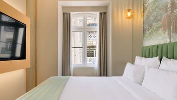 Quarto de hotel com cama, televisão na parede, janela com cortinas e luminária na parede.