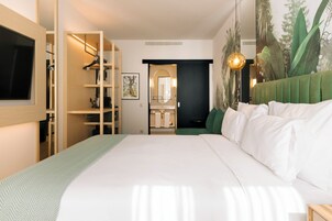 Quarto de hotel com uma cama grande, um guarda-roupa com espaço para pendurar, um espelho e uma cabeceira verde.