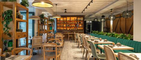 Restaurante com mobiliário de madeira, luminárias pendentes e área de estar acolchoada em tons de verde.