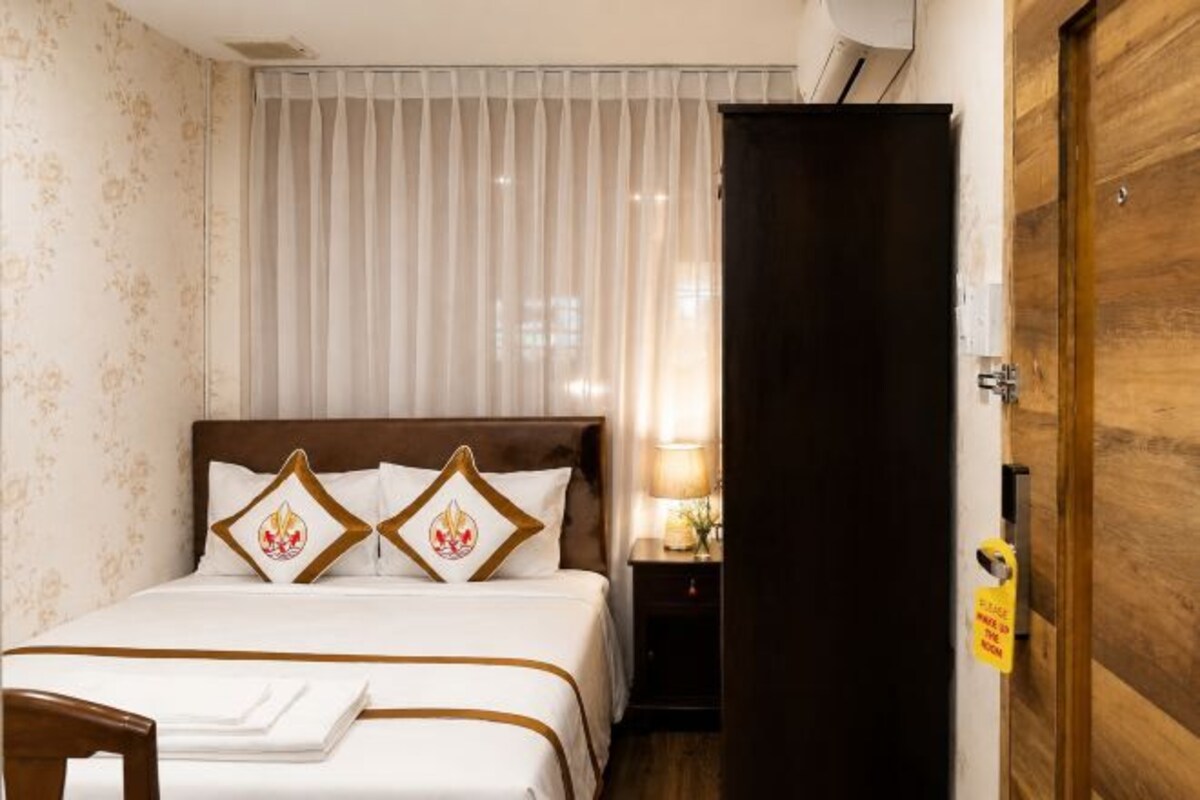 Quarto de hotel com uma cama, mesa de cabeceira e porta de madeira.