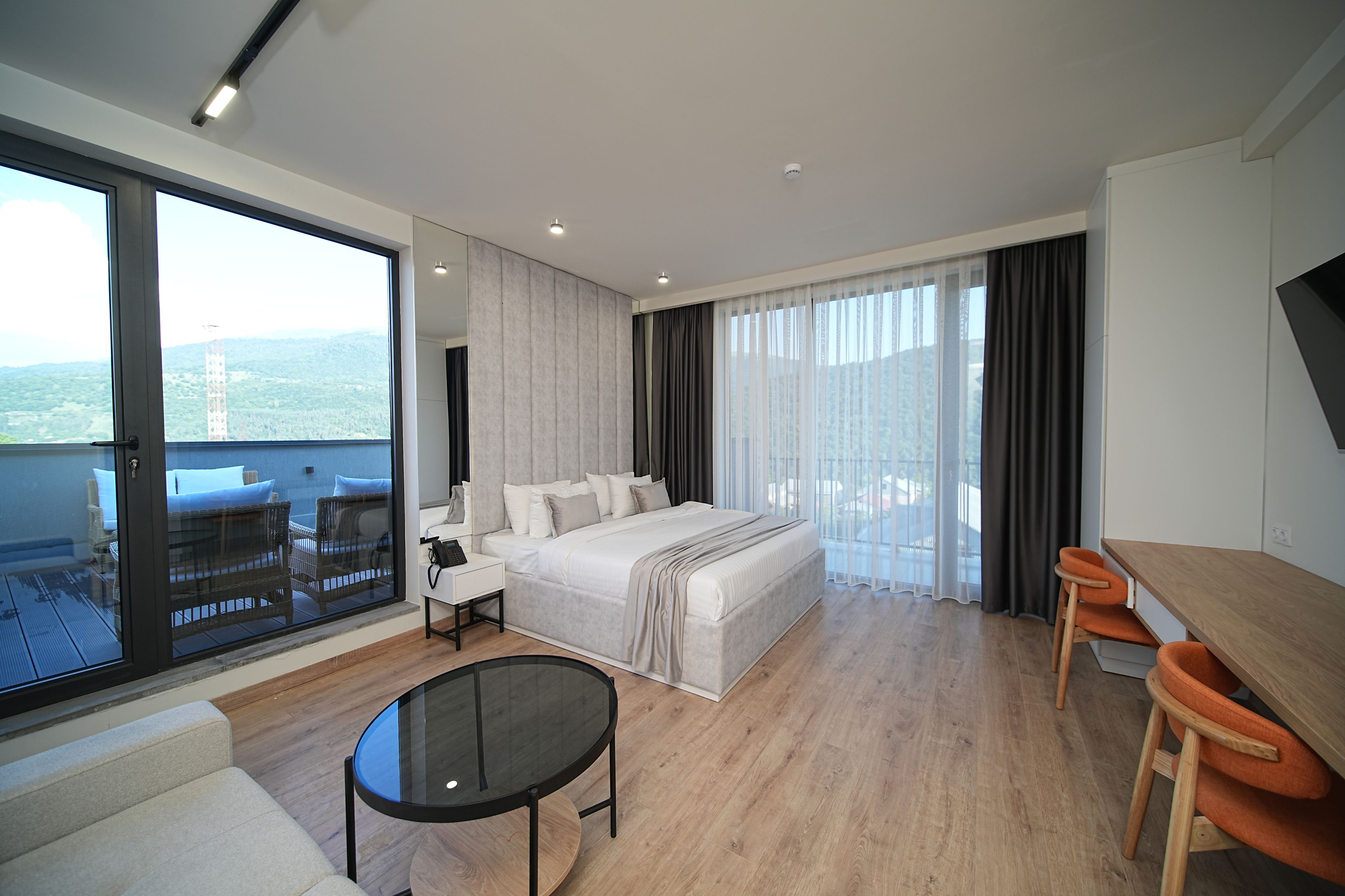 Quarto de hotel moderno com uma cama grande, escrivaninha, cadeira e varanda com mobiliário exterior.