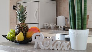 Uma cozinha com micro-ondas, cafeteira, fruteira e um vaso com planta.