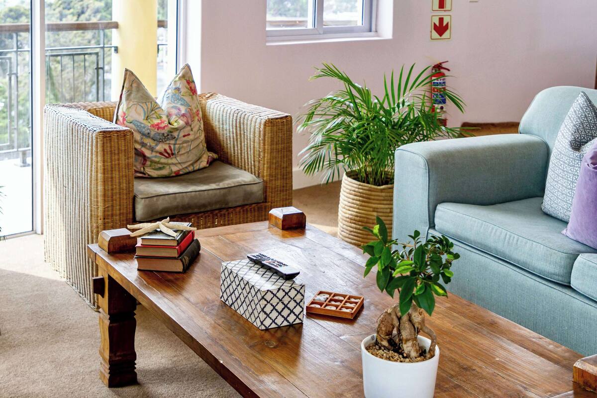 Uma sala de estar com uma mesa de centro de madeira, dois sofás, uma planta em vaso e uma estante de livros.