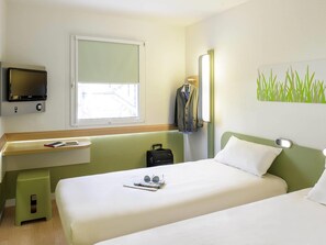 Quarto de hotel com uma cama, uma escrivaninha, uma televisão e uma janela.