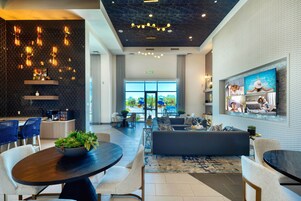 Um hall de hotel moderno com uma parede estampada escura, uma janela grande e uma área de estar com sofá e poltronas.